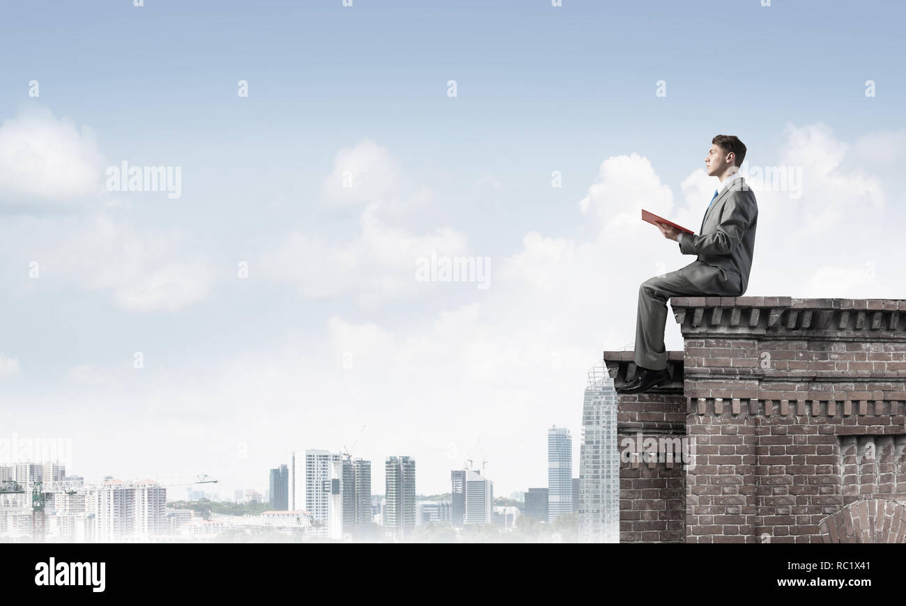 Man on roof edge reading book and cityscape at background Stock Photo ...