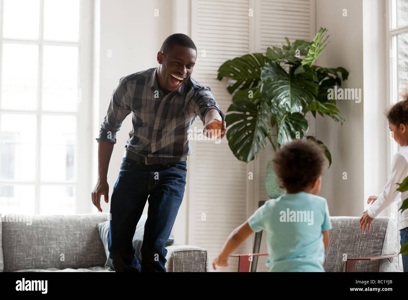 Happy african dad laughing running in living room catching kids Stock ...