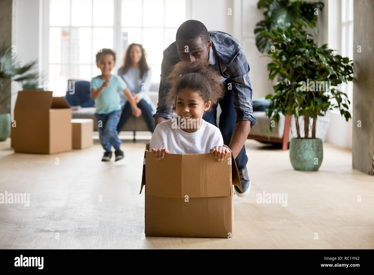 African dad playing with daughter riding in box, moving day Stock Photo ...