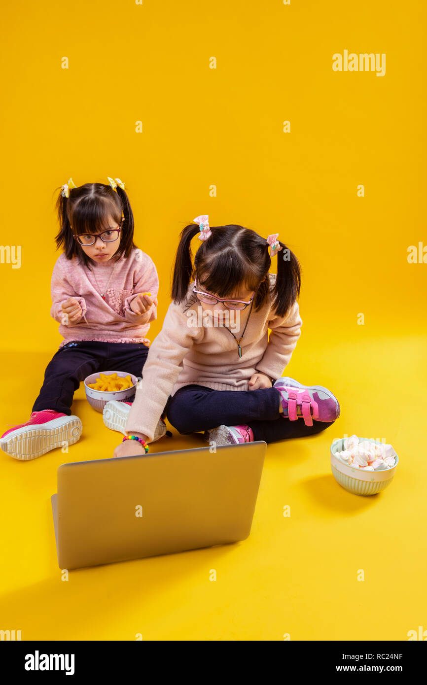 Curious small girls with genetic disorder spending time with laptop ...