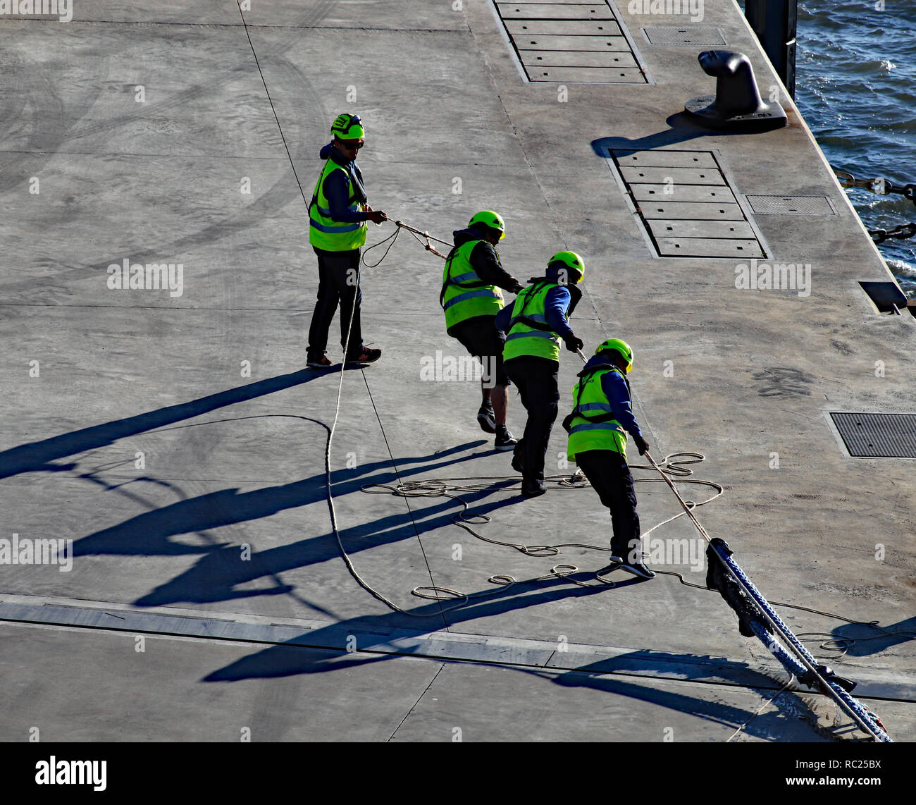Four port workers pulling a mooring rope ashore in Lisbon. Four port ...