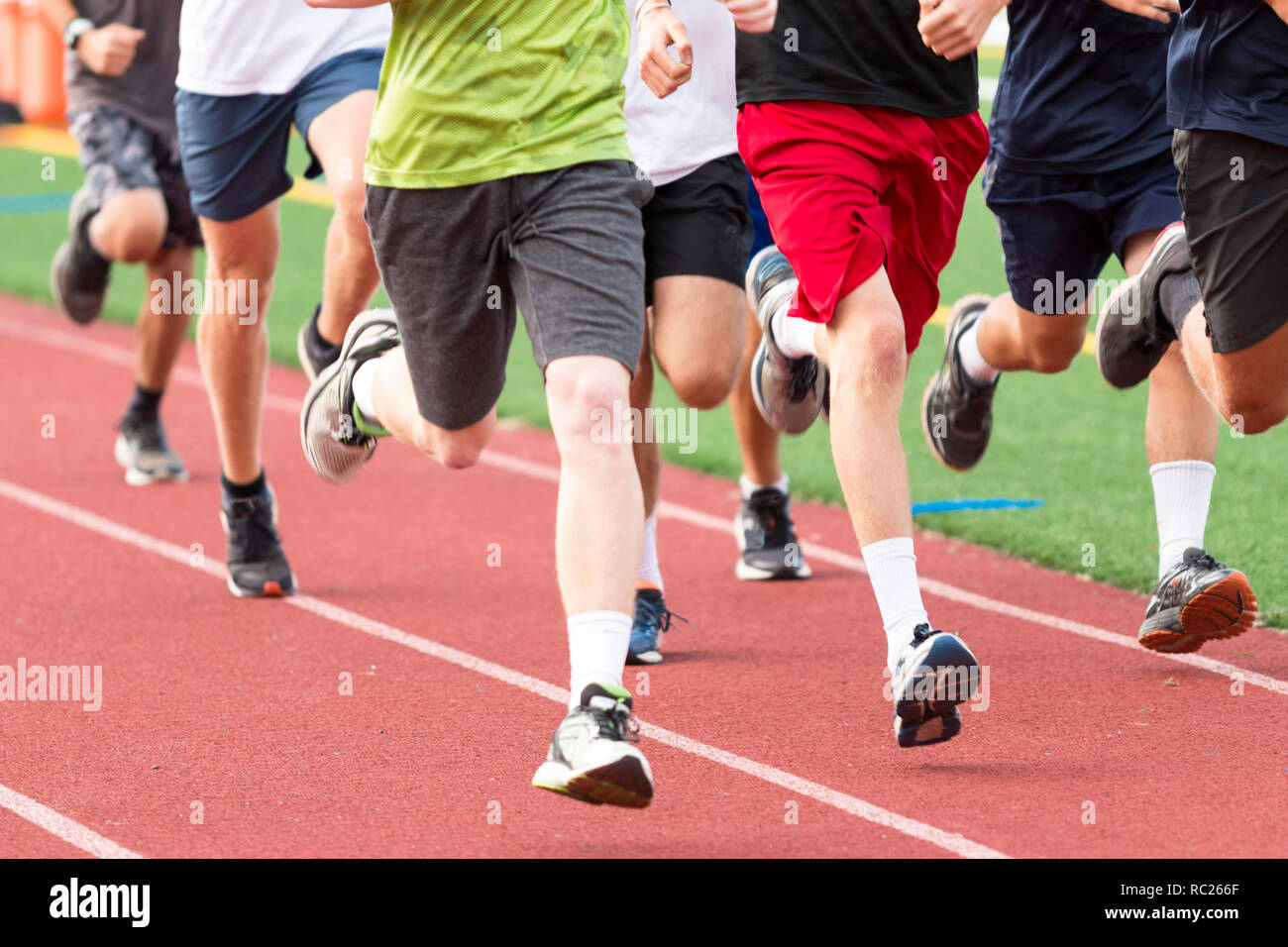 A group of high school boys running on a red track during practice ...