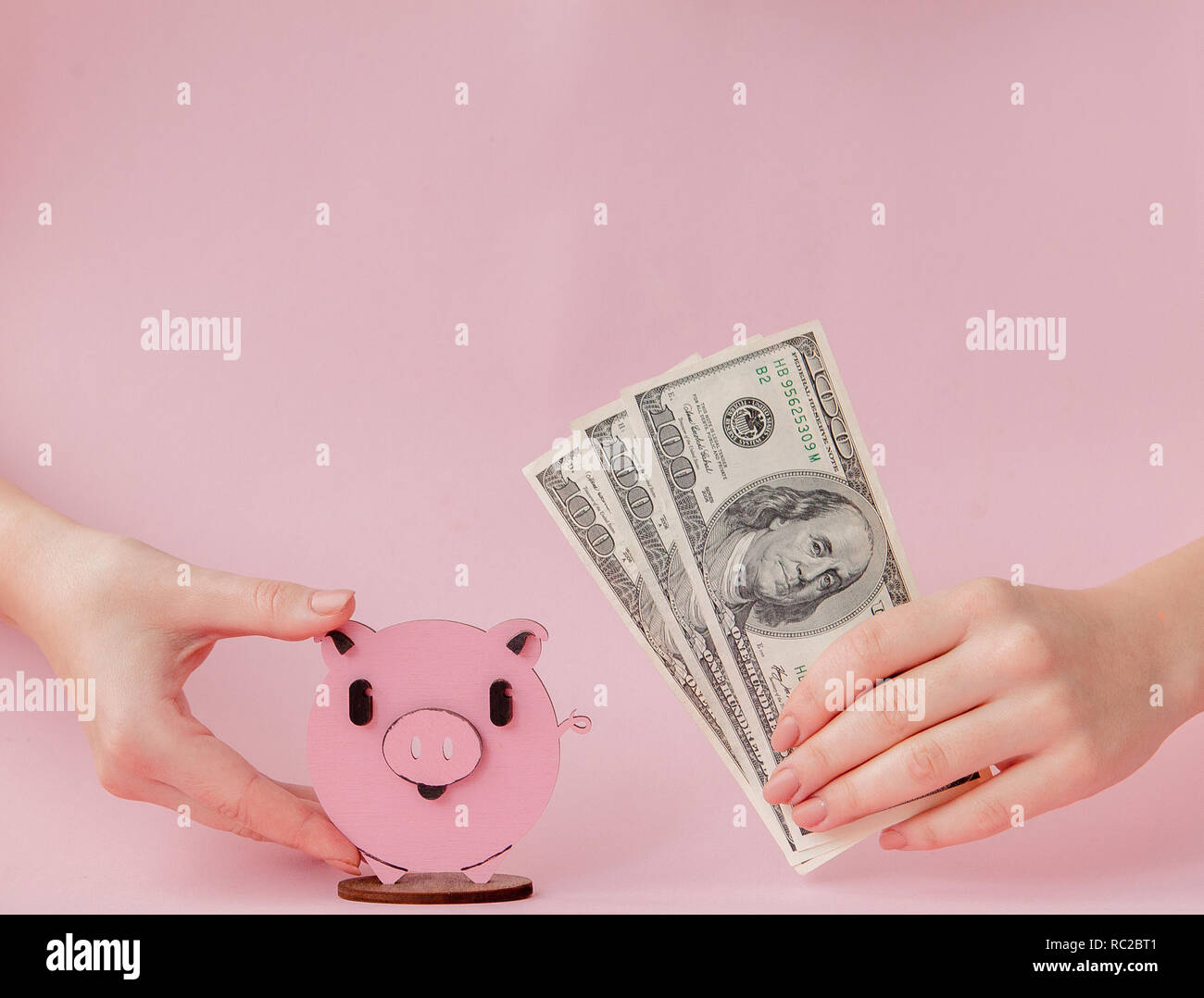Women's hands holding pink piggybank and dollar banknotes on pink ...