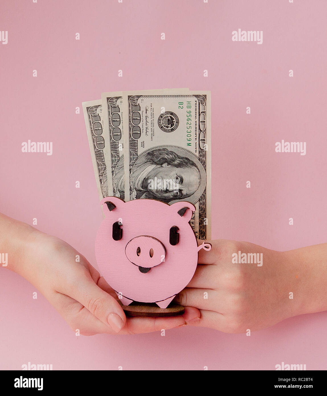 Women's hands holding pink piggybank and dollar banknotes on pink ...