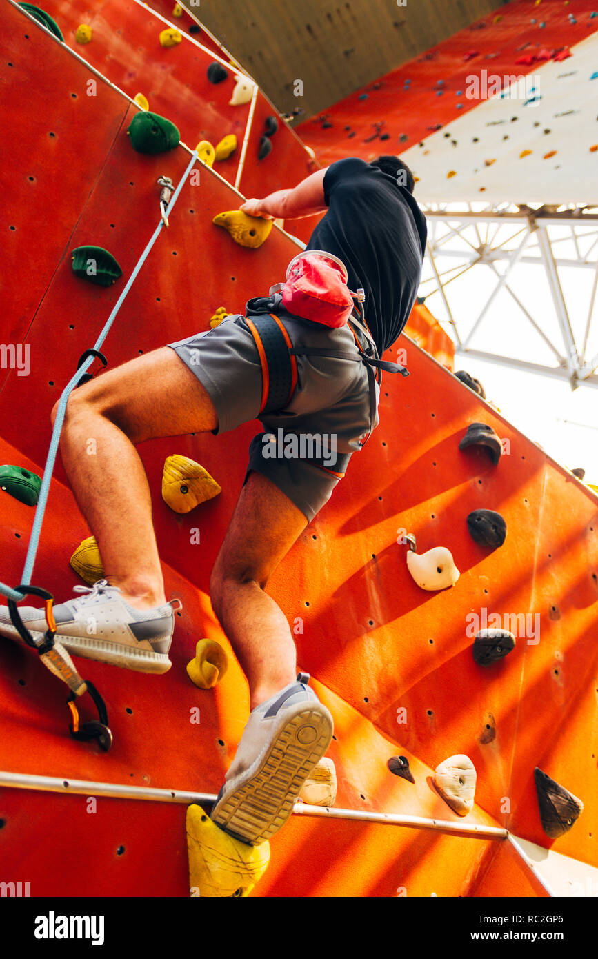 Man wearing belaying rope, climbing on a very high rock climbing wall ...