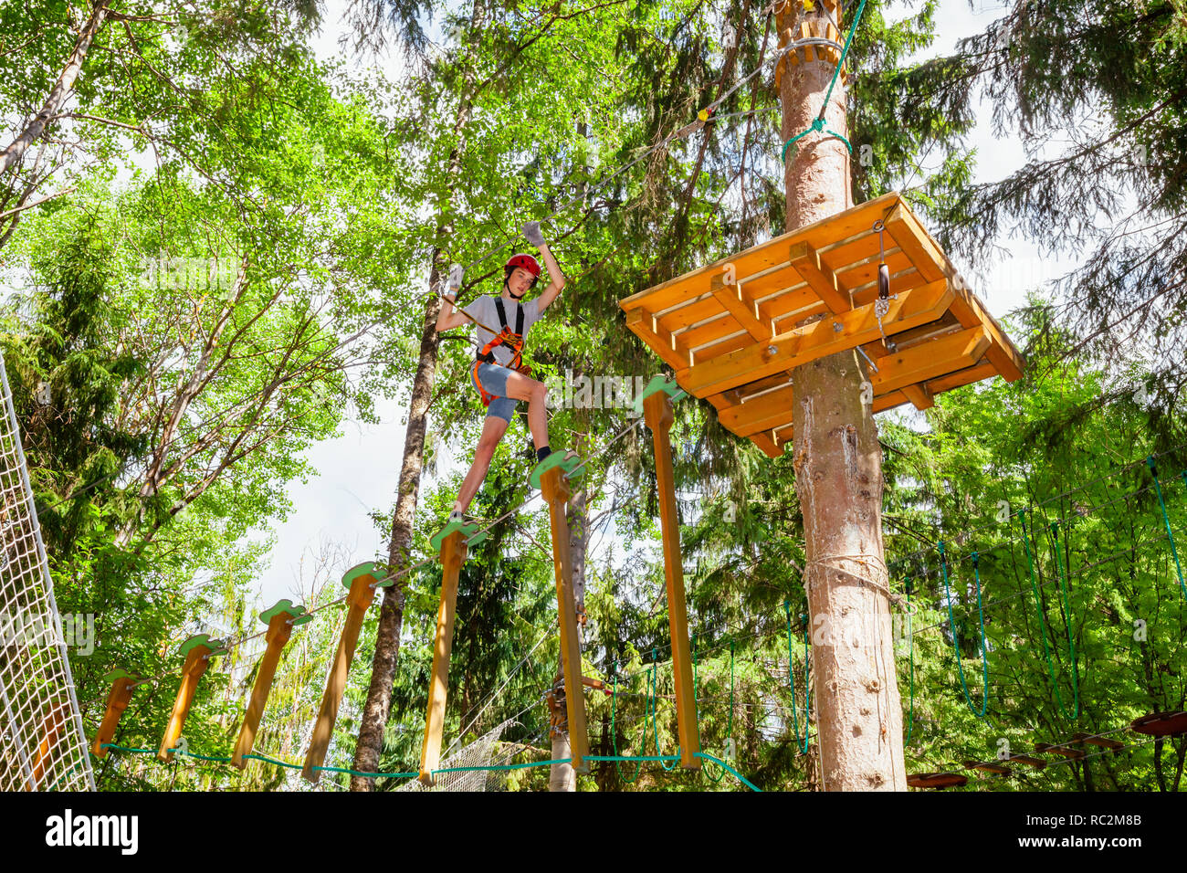 Teenager boy wearing safety harness passing hanging rope bridge ...