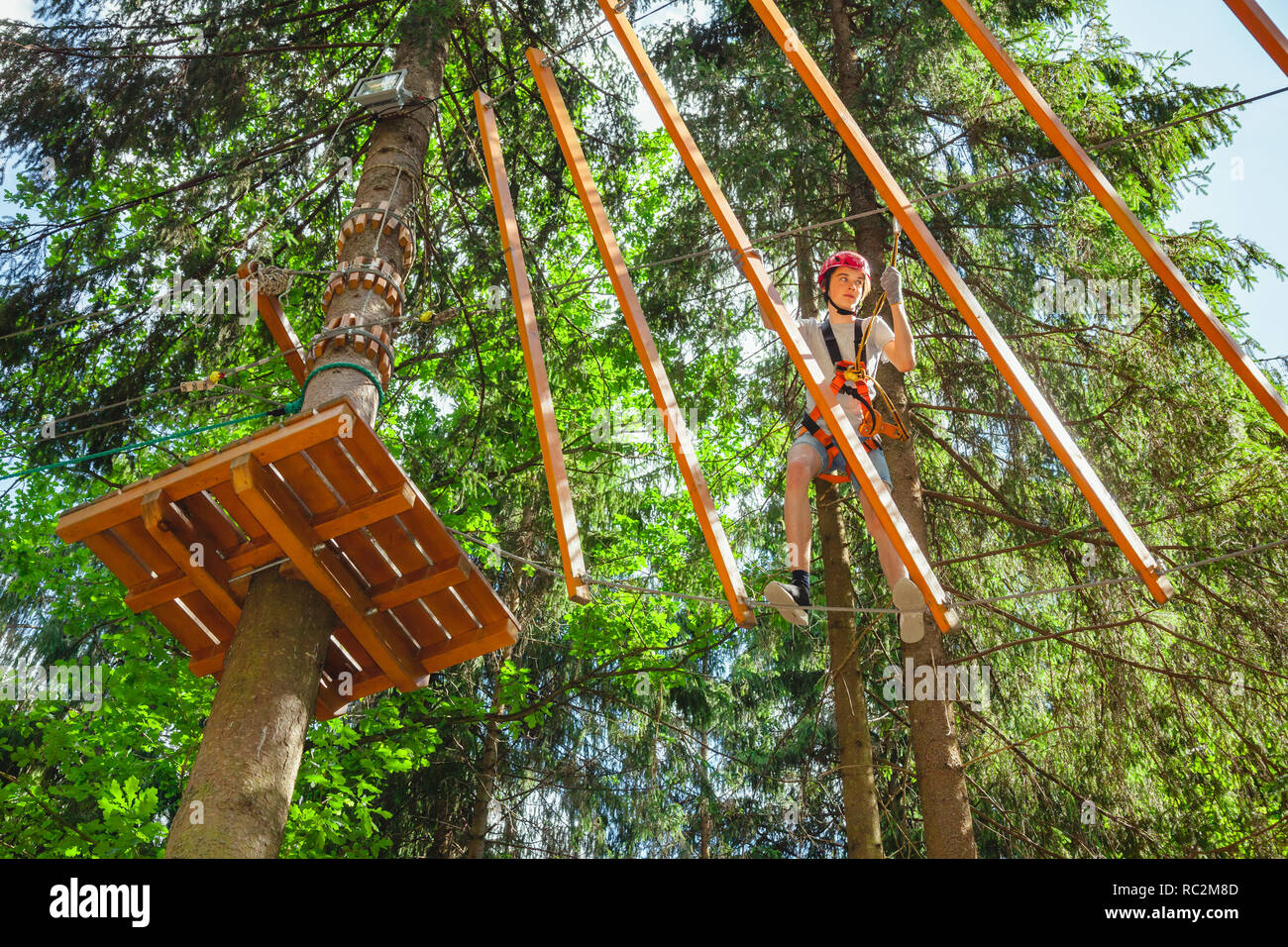 Teenager boy wearing safety harness passing hanging rope bridge ...