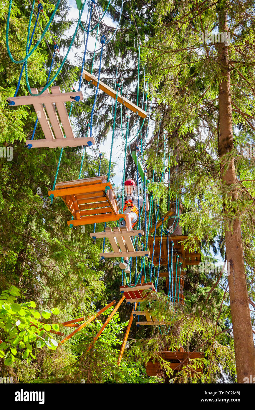 Teenager boy wearing safety harness passing hanging rope bridge ...