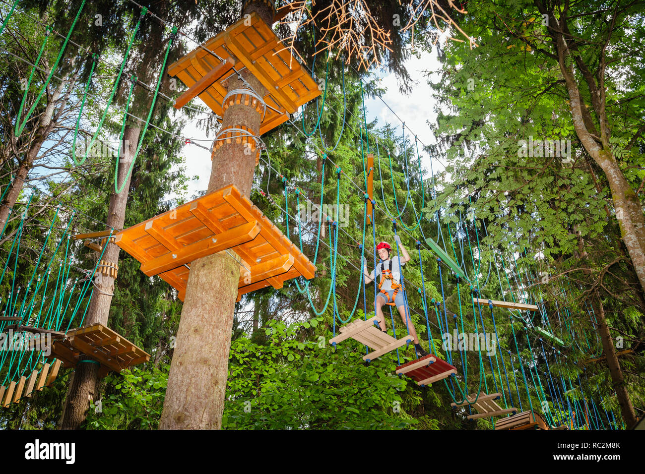 Teenager boy wearing safety harness passing hanging rope bridge ...