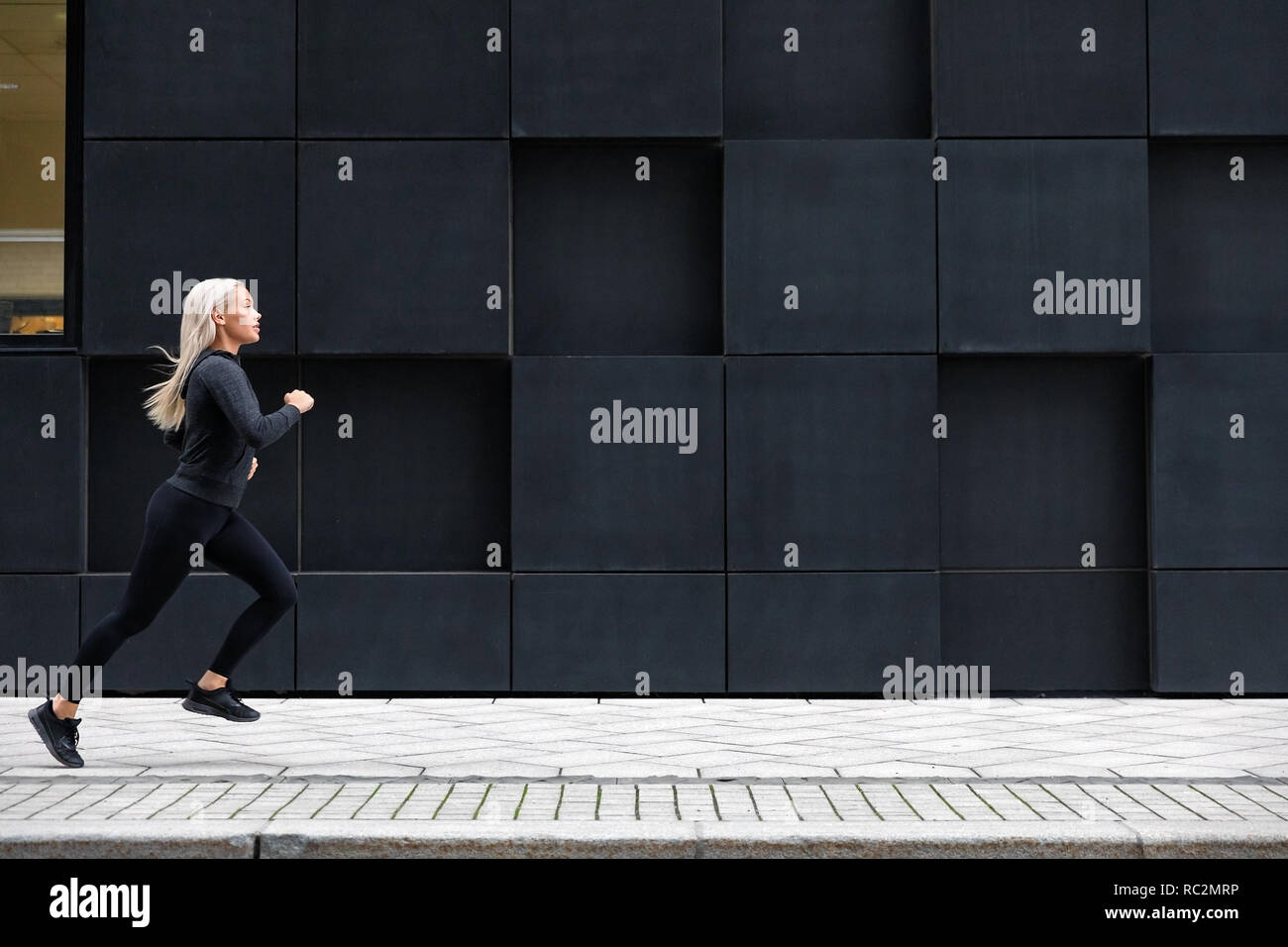 Female runner jogging on the city street against modern city walls ...
