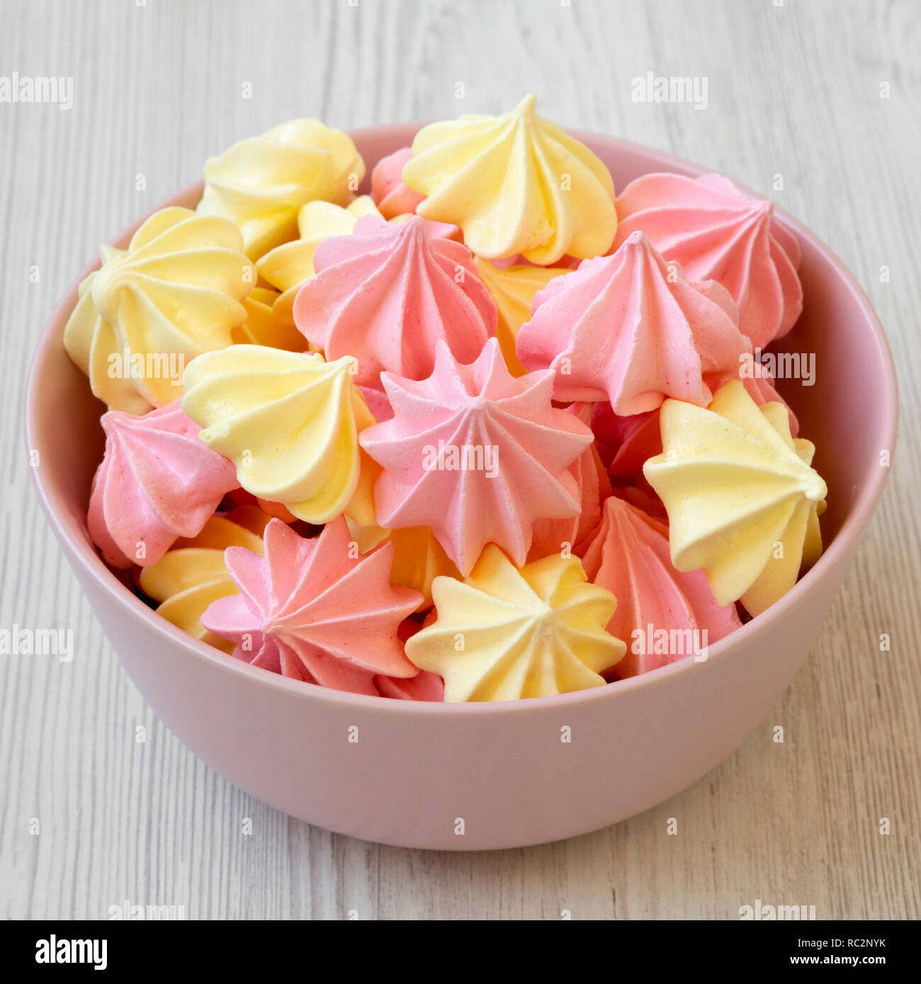 Mini meringues in a pink bowl over white wooden surface, side view ...