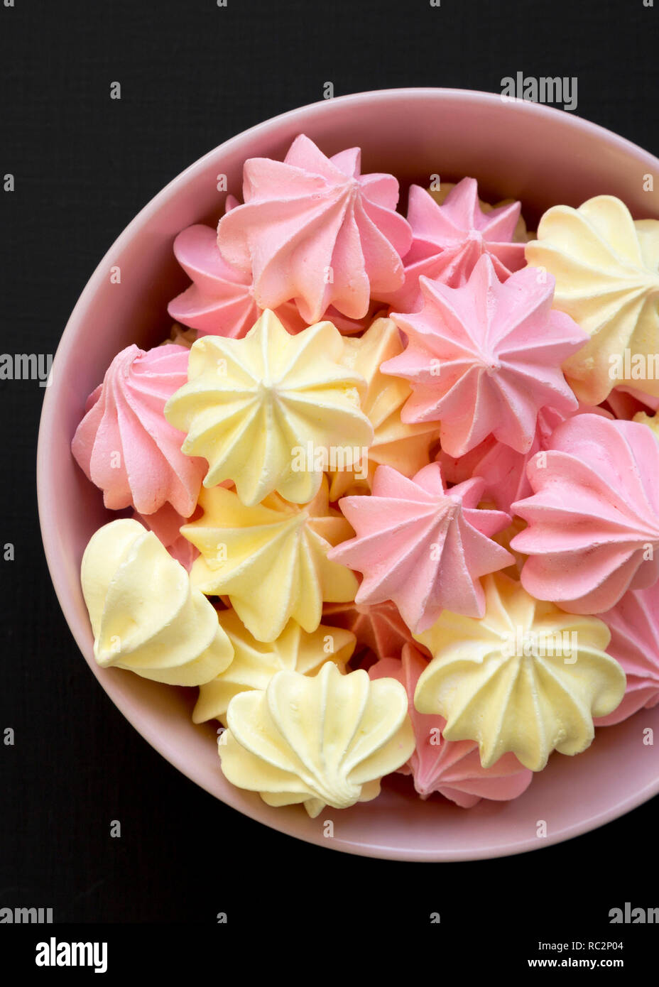 Mini meringues in a pink bowl over black surface, top view. From above ...