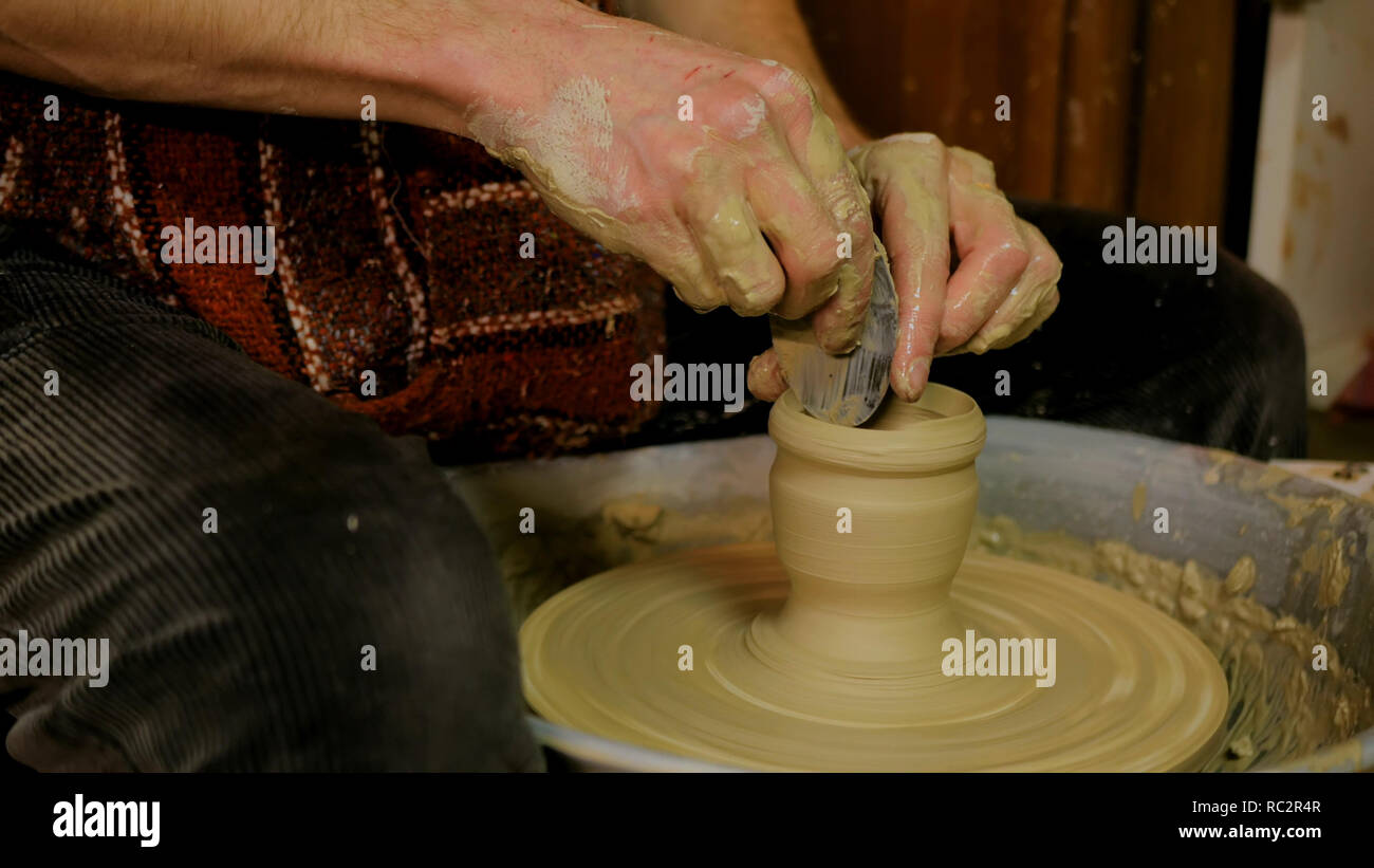 Professional male potter shaping mug with special tool in pottery ...