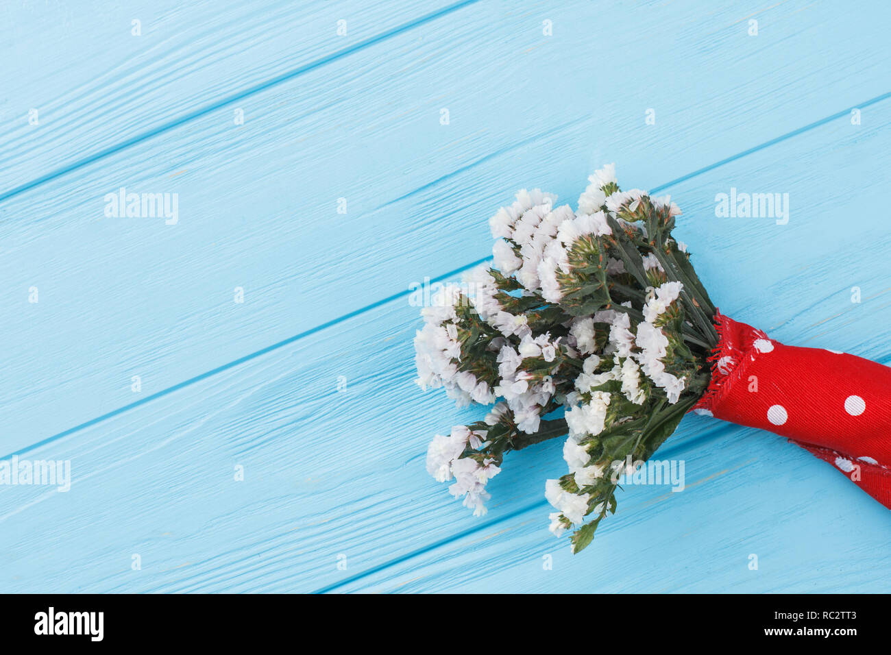 Statice white flowers bouquet wraped in red tissue. Blue wooden table ...