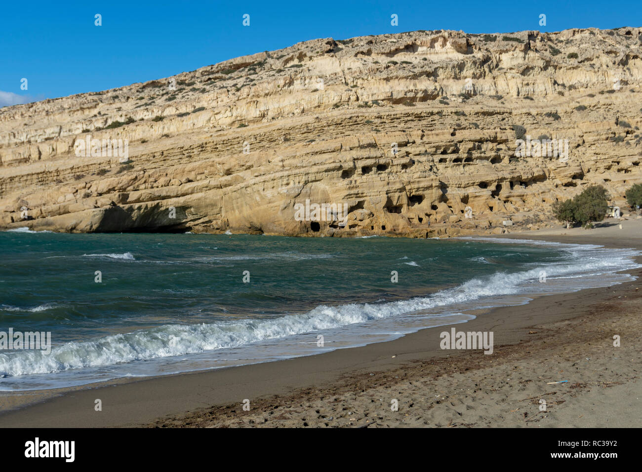 Beach with sand and waves and a cliff with old caves in background ...