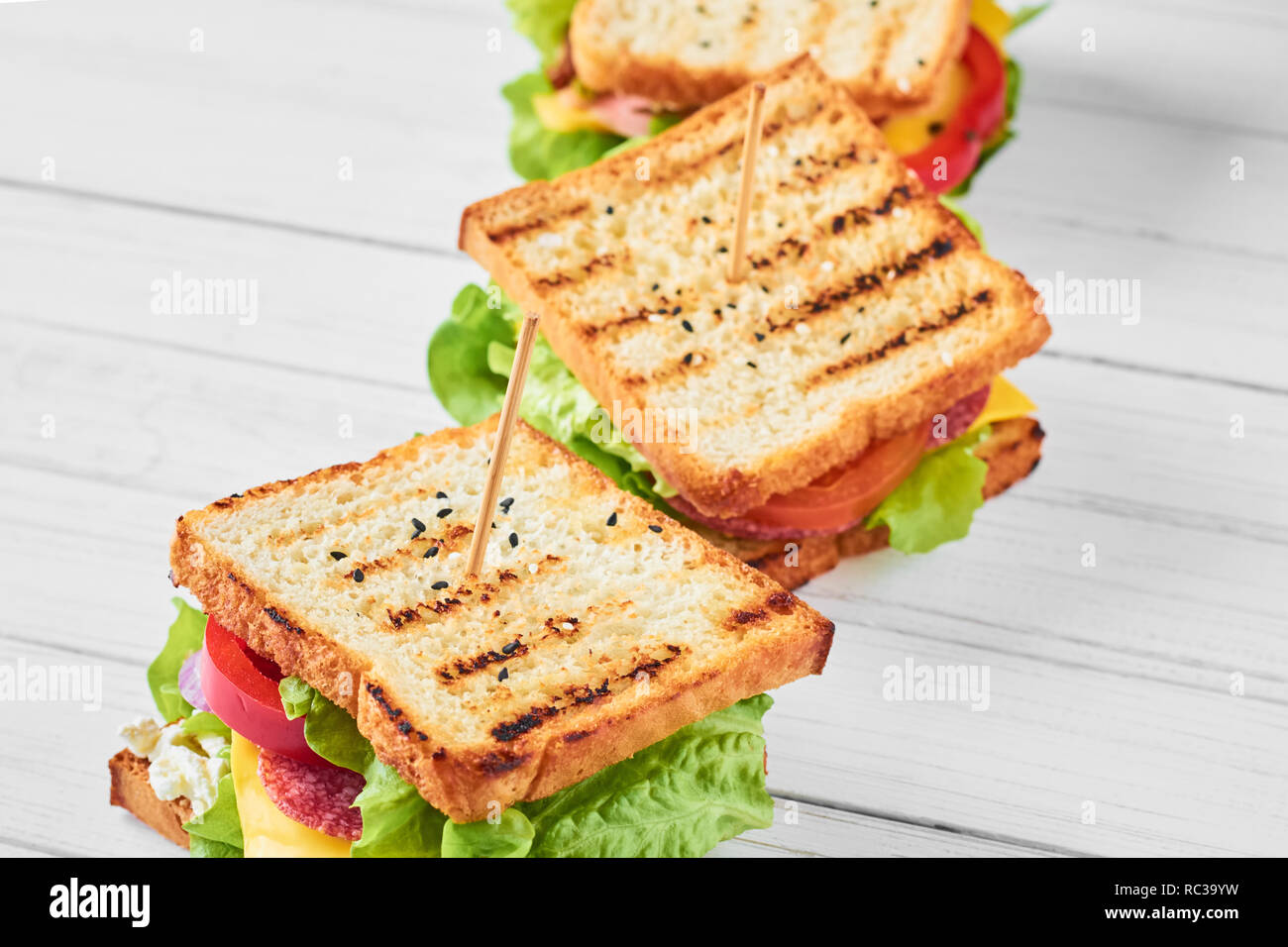 Three sandwiches with ham, lettuce and fresh vegetables on white ...