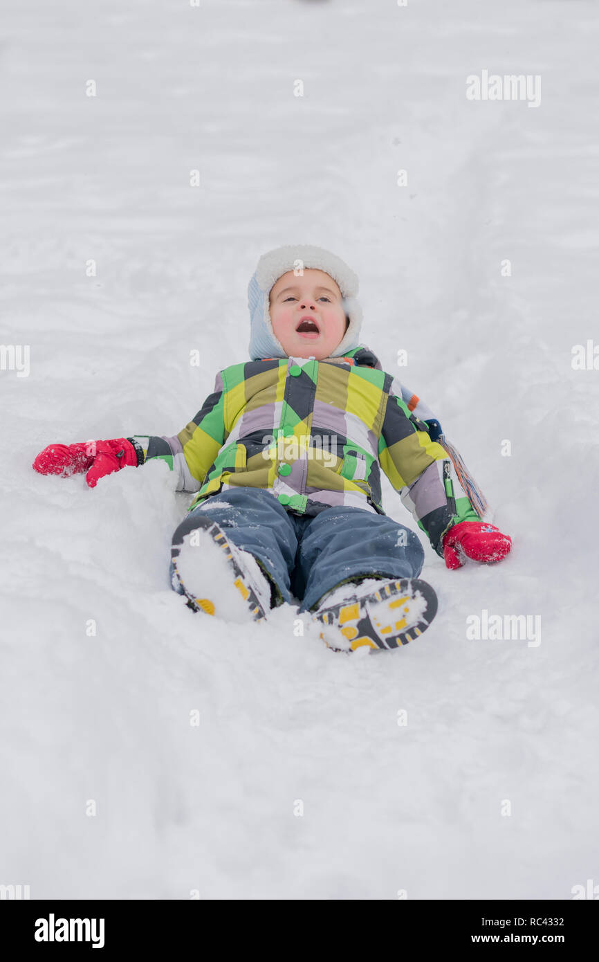 Little boy child playing with snow and having fun lying on snowy field ...