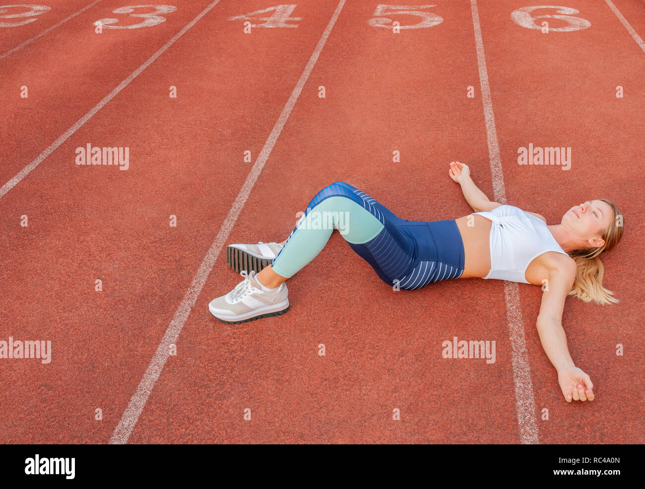 Tired woman runner taking a rest after run lying on the running track ...