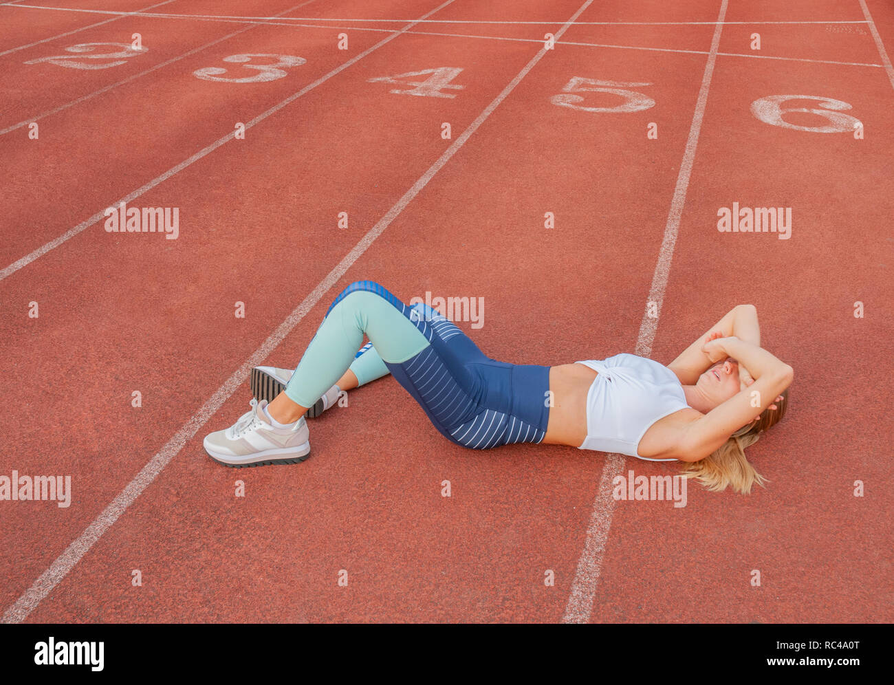 Tired woman runner taking a rest after run lying on the running track ...