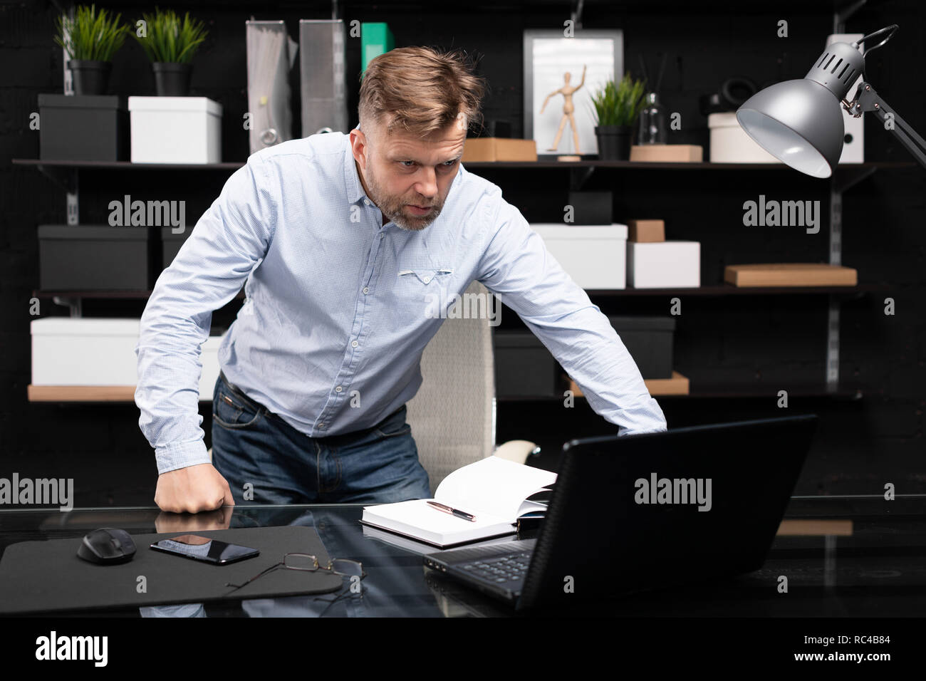 young man stands near the computer table and looks at the monitor Stock ...