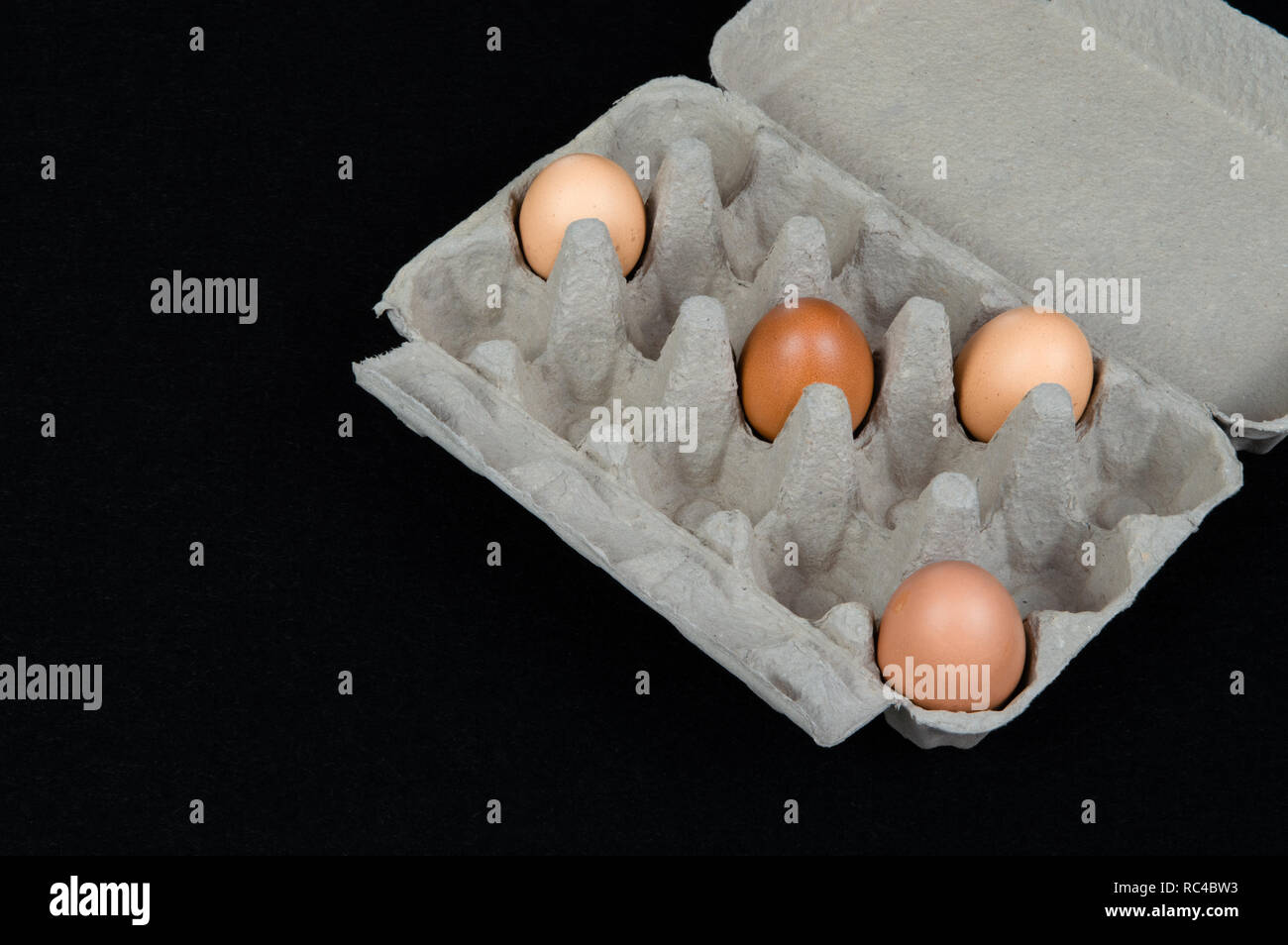 Four chicken eggs in a carton box, isolated on black felt background ...