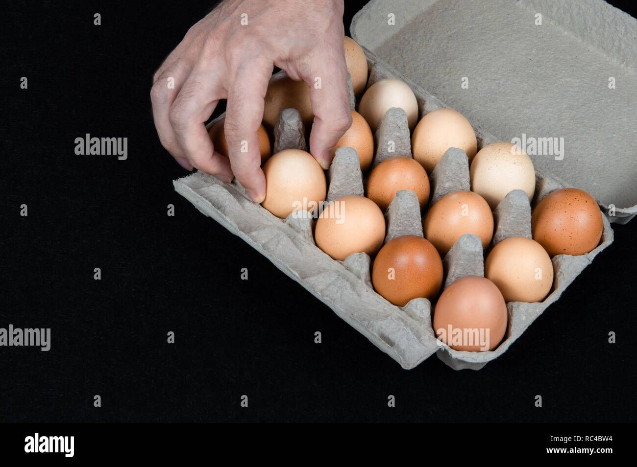 Male hand taking one egg from cardboard egg box on black felt ...