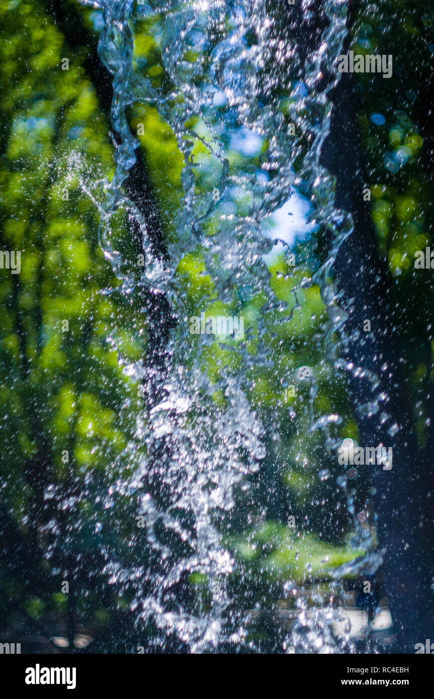transparent falling water vertical flows against a blue sky and green ...