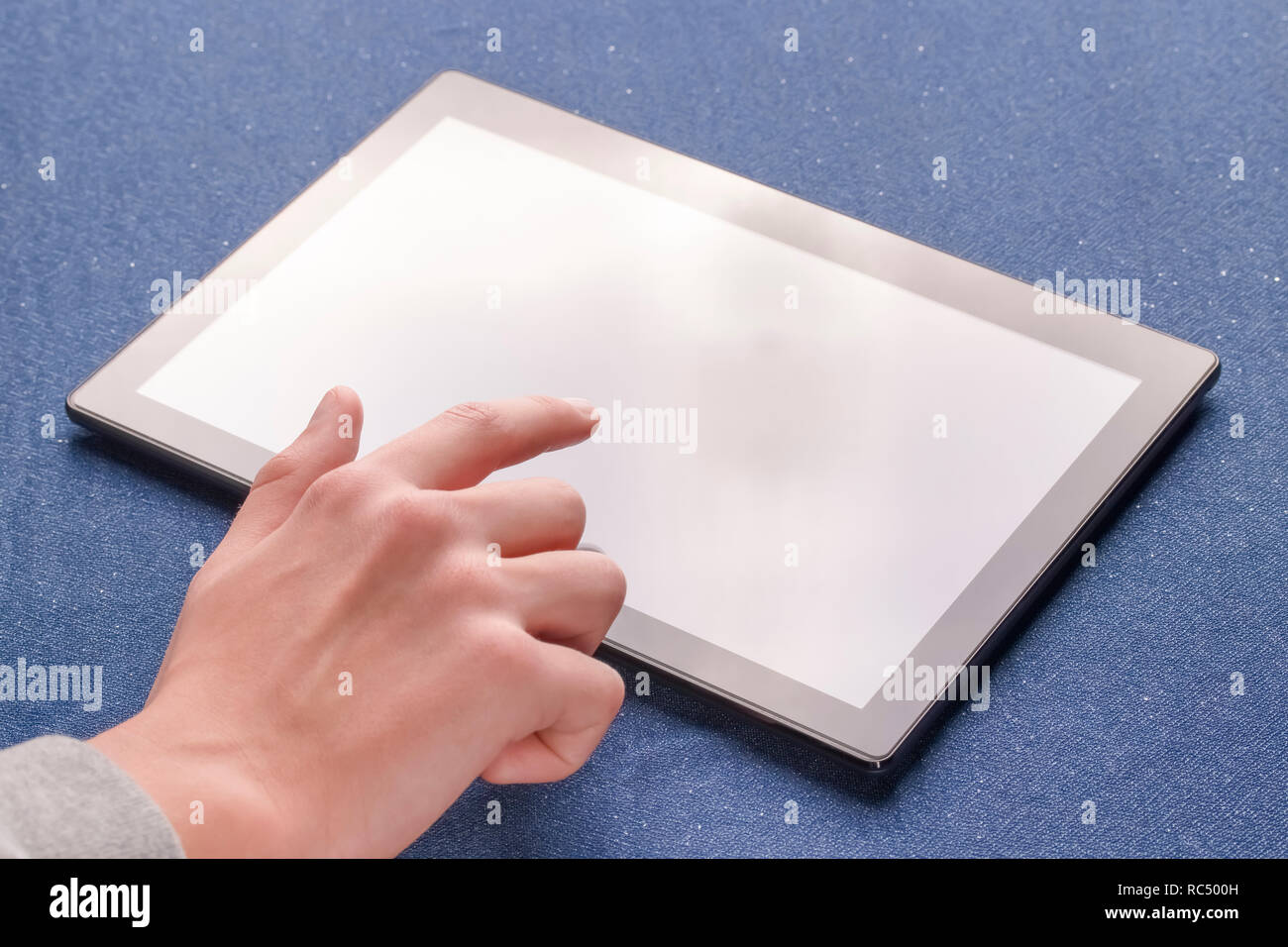 Hands use a brightly lit black tablet on a blue cloth sheet Stock Photo ...