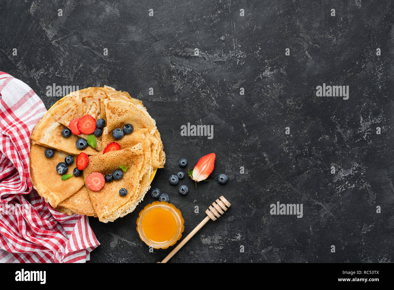 Tasty homemade crepes with honey and berries on black concrete ...