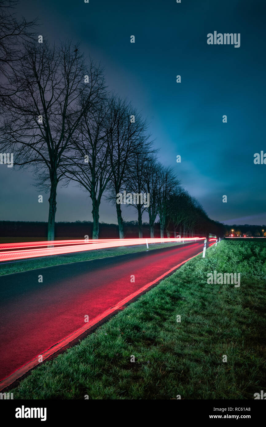 A country road with a moving car with shining red lights at night Stock ...