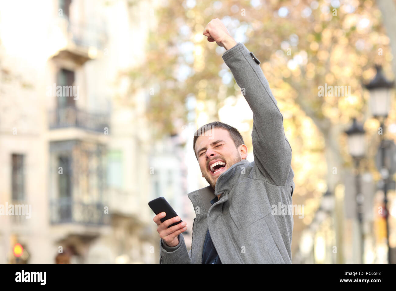 Portrait of an excited man holding smart phone and raising arm in the ...