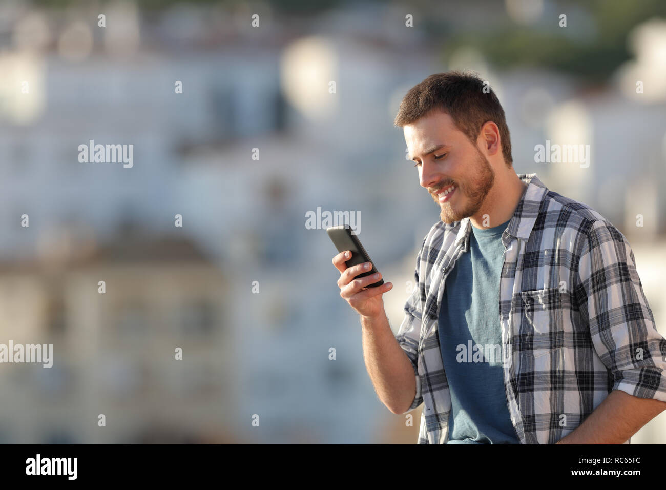 Happy man checking smart phone text in a town at sunset Stock Photo - Alamy
