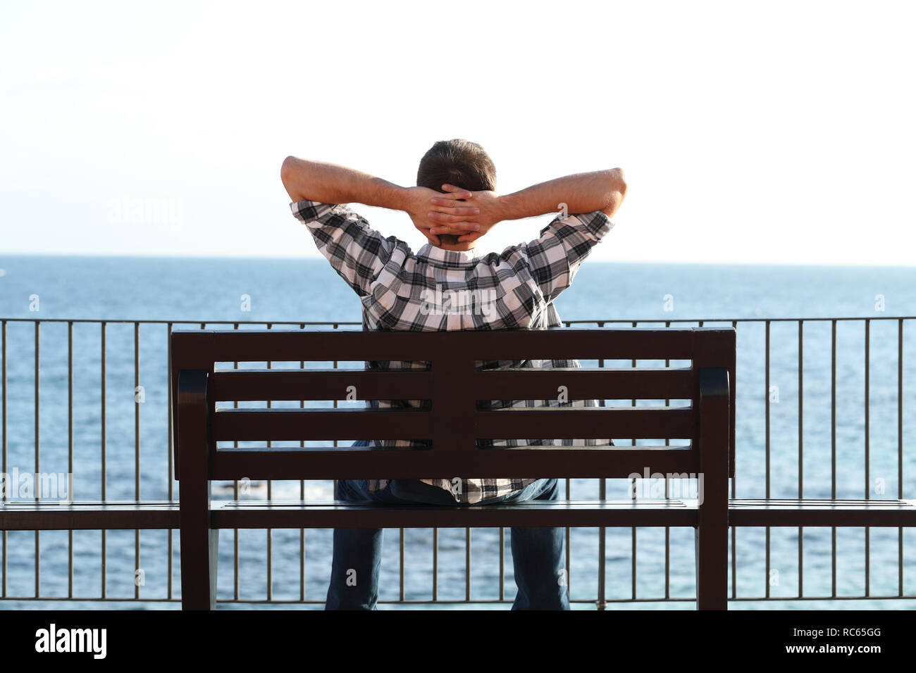 Back view portrait of a man relaxing on the beach sitting on a bench ...