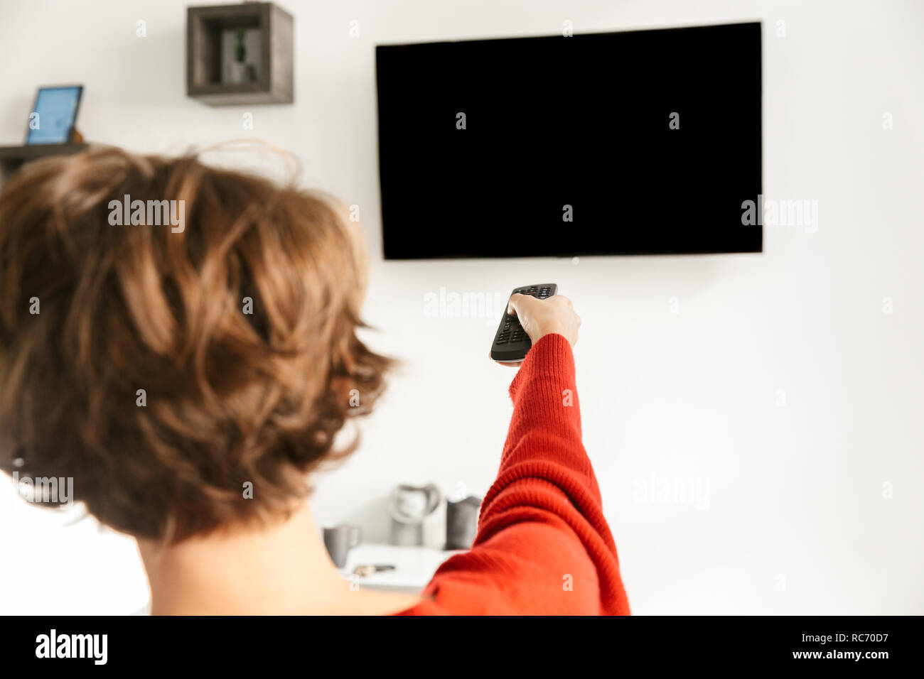 Back view of a woman sitting on a couch, holding remote control infront ...