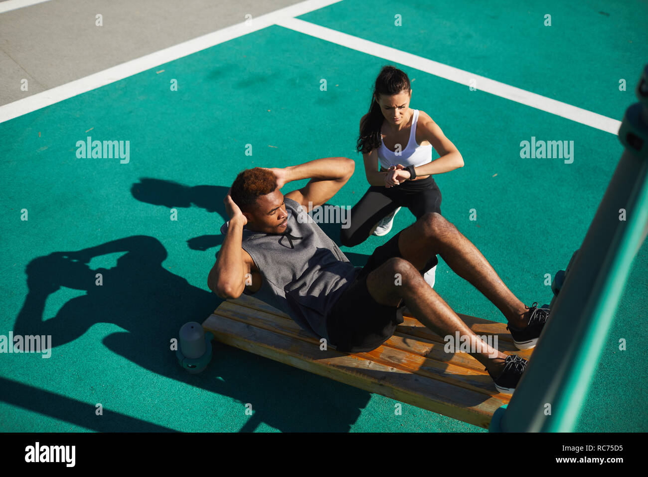 Lady coach keeping time while man doing crunches Stock Photo - Alamy