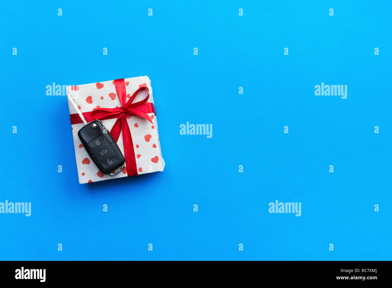 Car key on paper gift box with red ribbon bow and heart on blue table ...