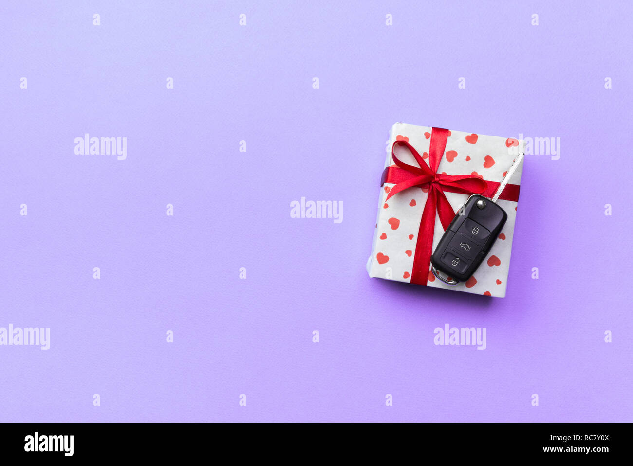 Car key on paper gift box with red ribbon bow and heart on violet table ...