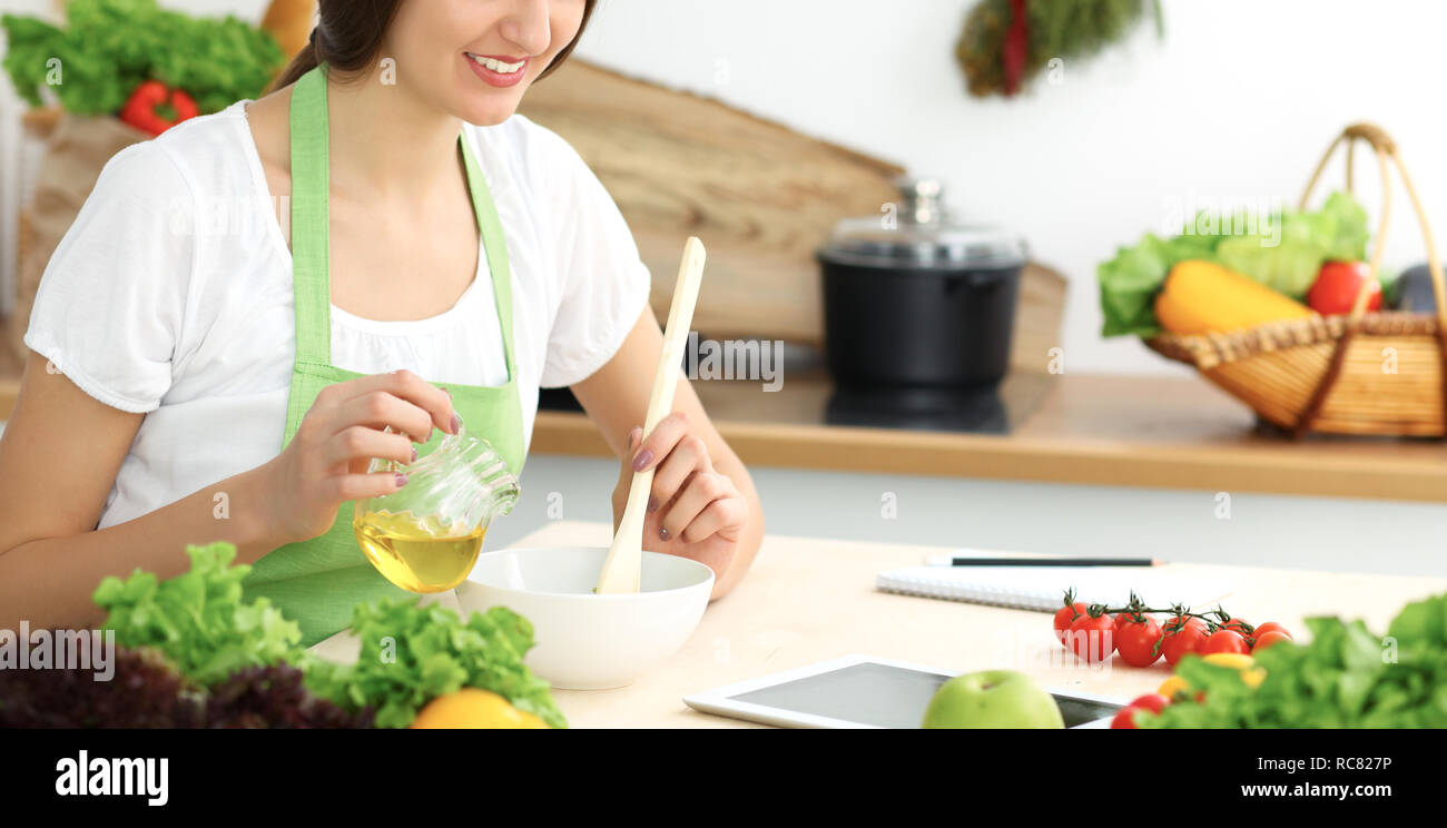 Beautiful Hispanic woman cooking in kitchen while using tablet computer ...
