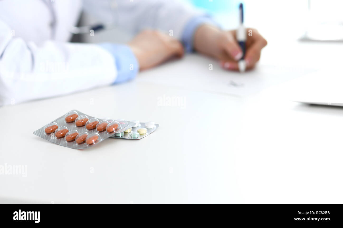 Female doctor filling up prescription form while sitting at the desk in ...