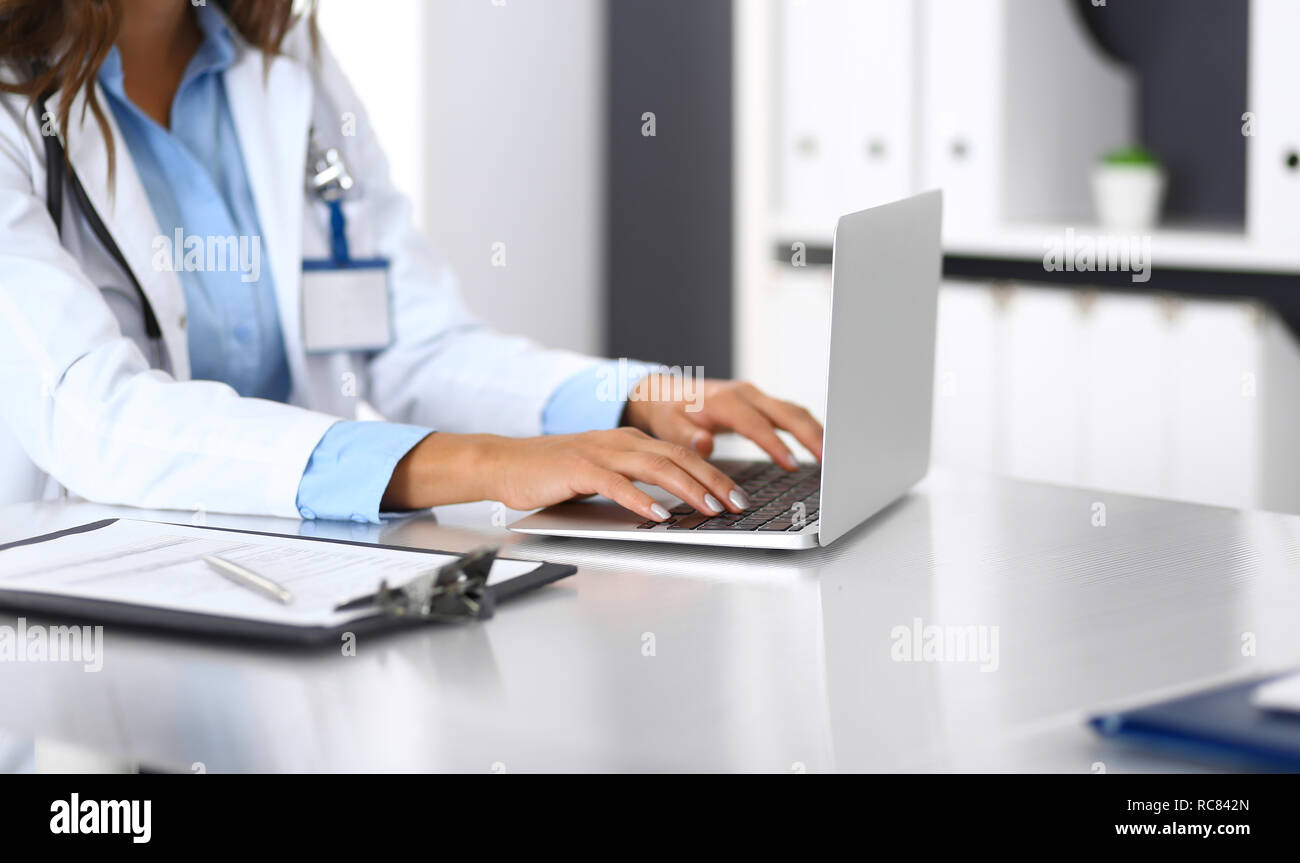 Unknown doctor woman typing on laptop computer while sitting at the ...