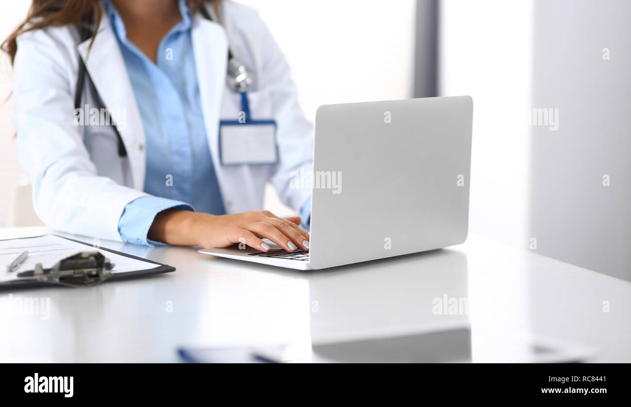 Unknown doctor woman typing on laptop computer while sitting at the ...