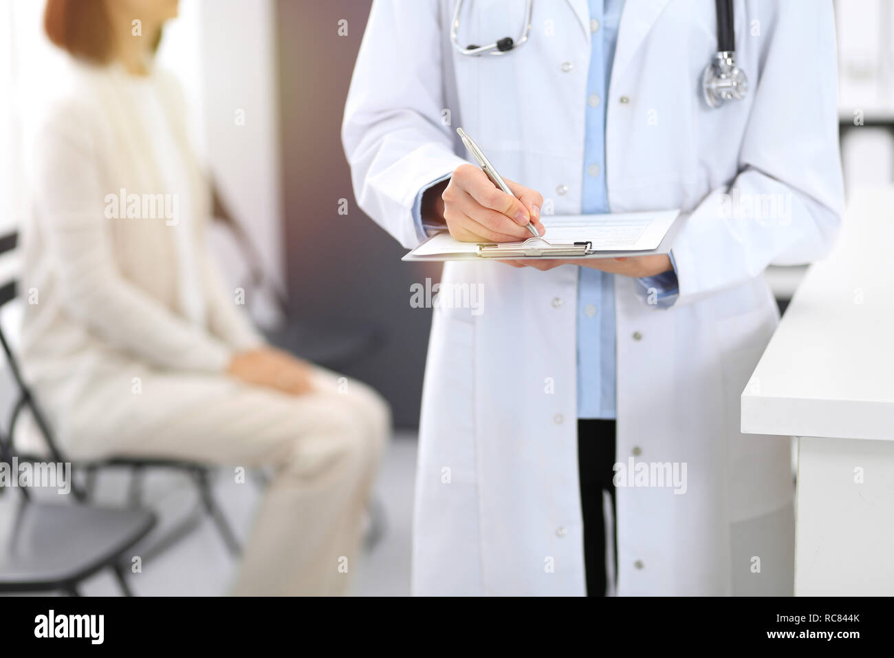 Doctor woman filling up medical form while standing near reception desk ...