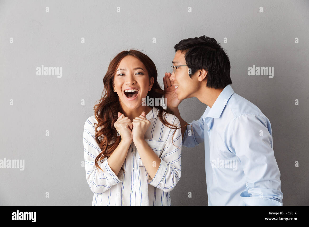 Excited asian couple standing isolated over gray background, telling ...