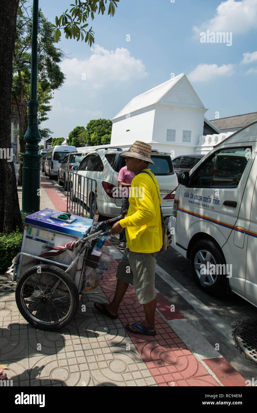 Bangkok local in national dress push barrow near parked cars wearing a ...