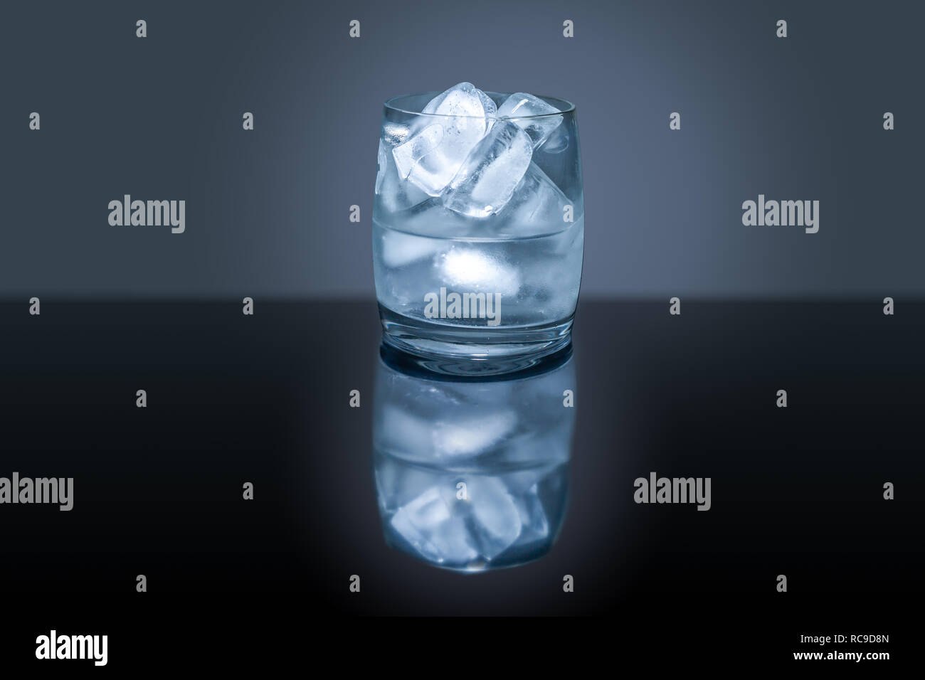 Glass with ice cubes and water on reflecting table with dark background Stock Photo - Alamy