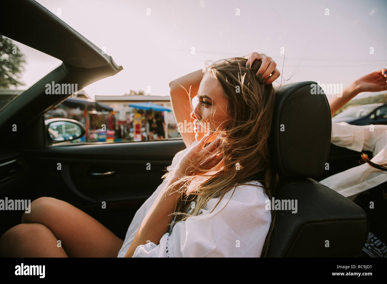 Two happy female friends driving in white cabriolet car and looking for ...