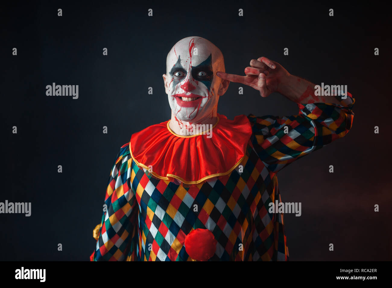 Portrait of mad bloody clown twirls finger to his temple, face in blood ...