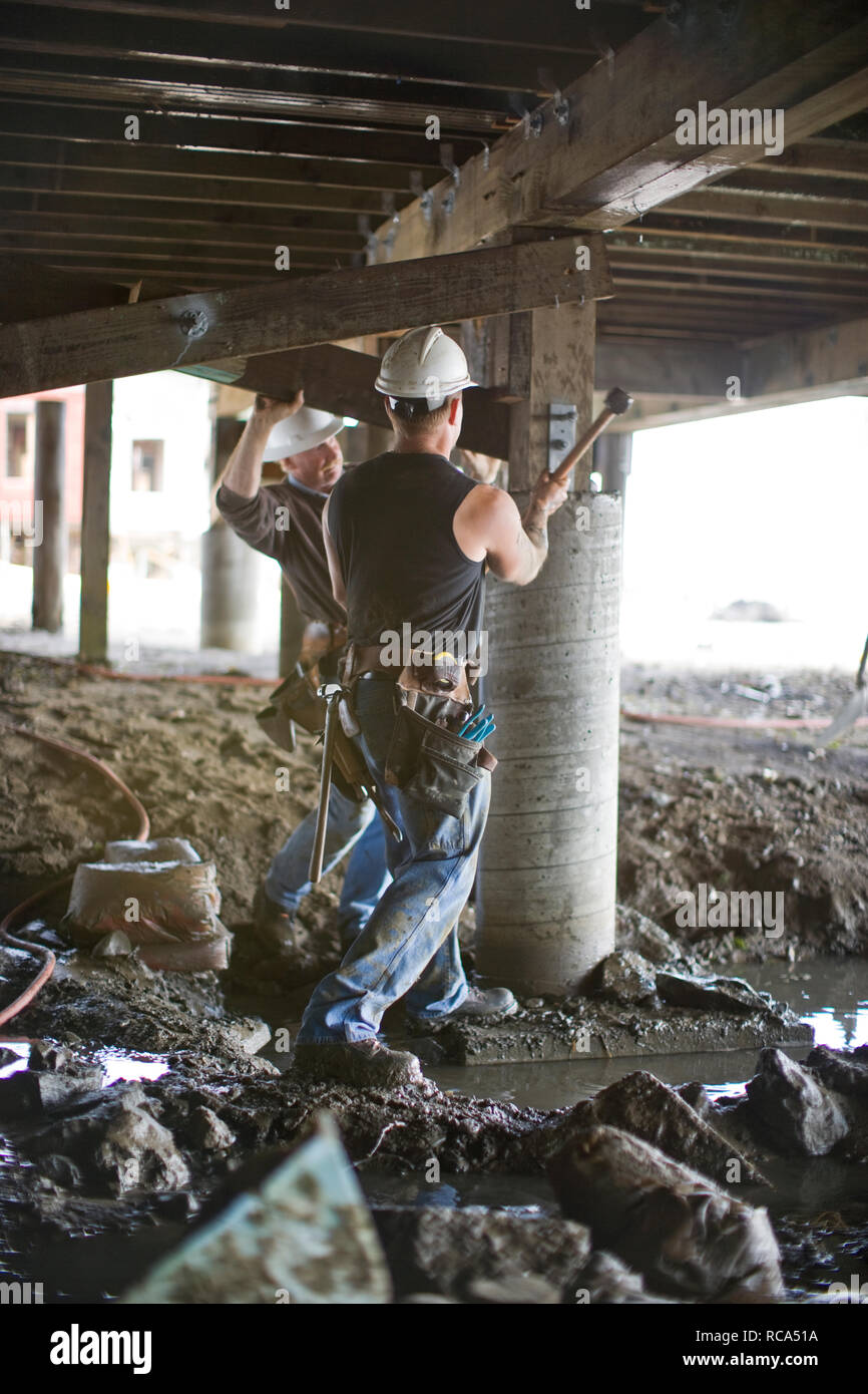 Two male construction workers working underneath a building on a ...