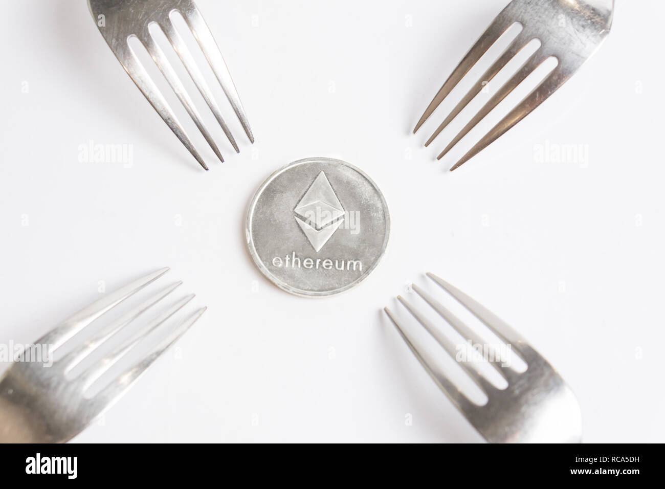 Ethereum cryptocurreny silver coin placed between forks on white ...