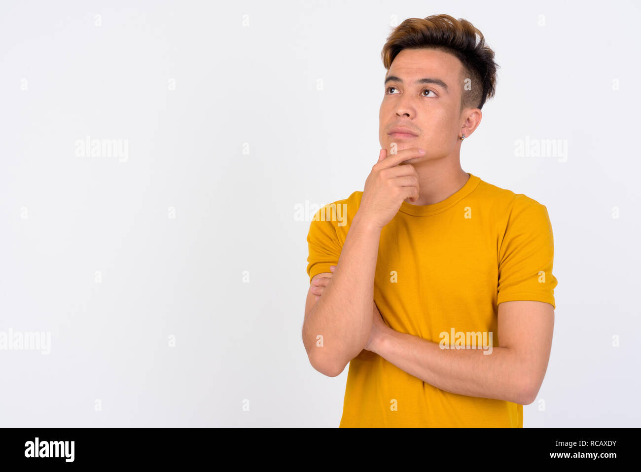 Portrait of young Asian man thinking and looking upagainst white ...